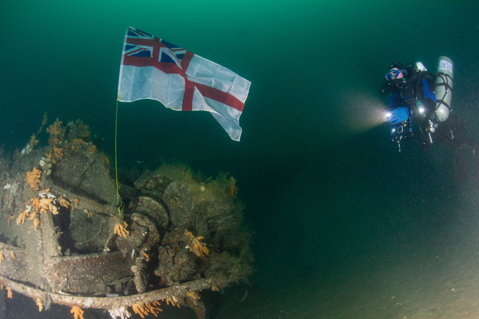 Lt Cdr Jen Smith shines her torch on the White Ensign over the wreck of ...